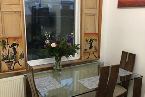 Uma sala de jantar com mesa de vidro, cadeiras e um vaso com flores.
