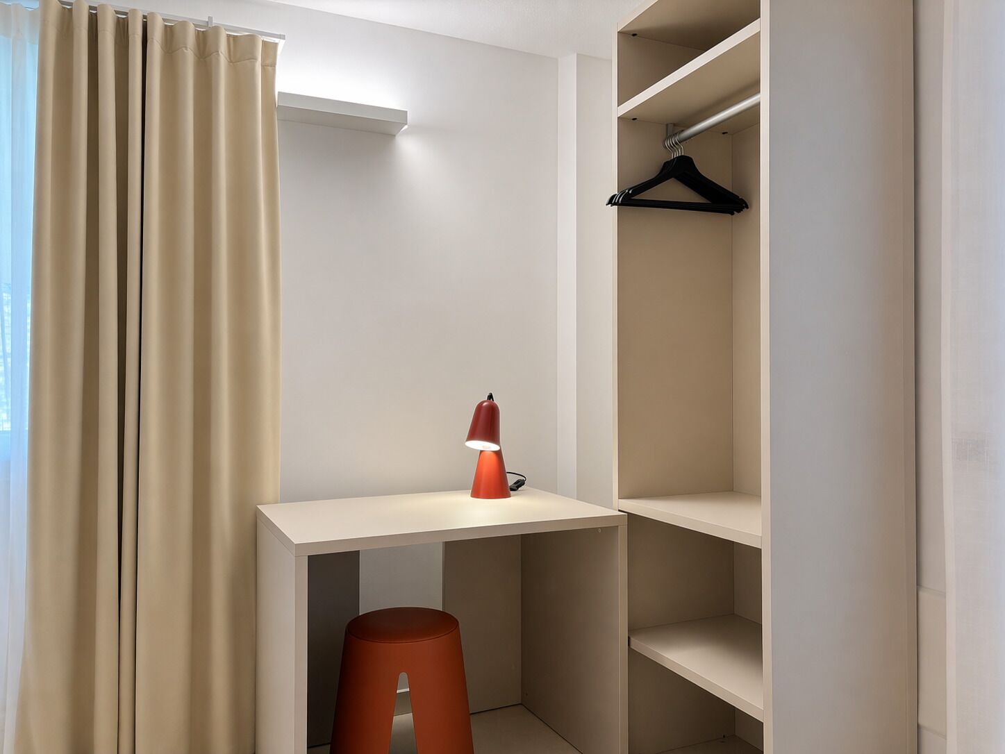 Quarto com escrivaninha, luminária pendente, um banquinho e guarda-roupa.