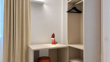 Quarto com escrivaninha, luminária pendente, um banquinho e guarda-roupa.