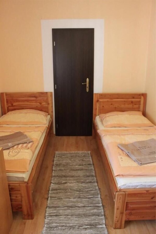 Quarto com duas camas de madeira, uma porta escura e um tapete estreito.