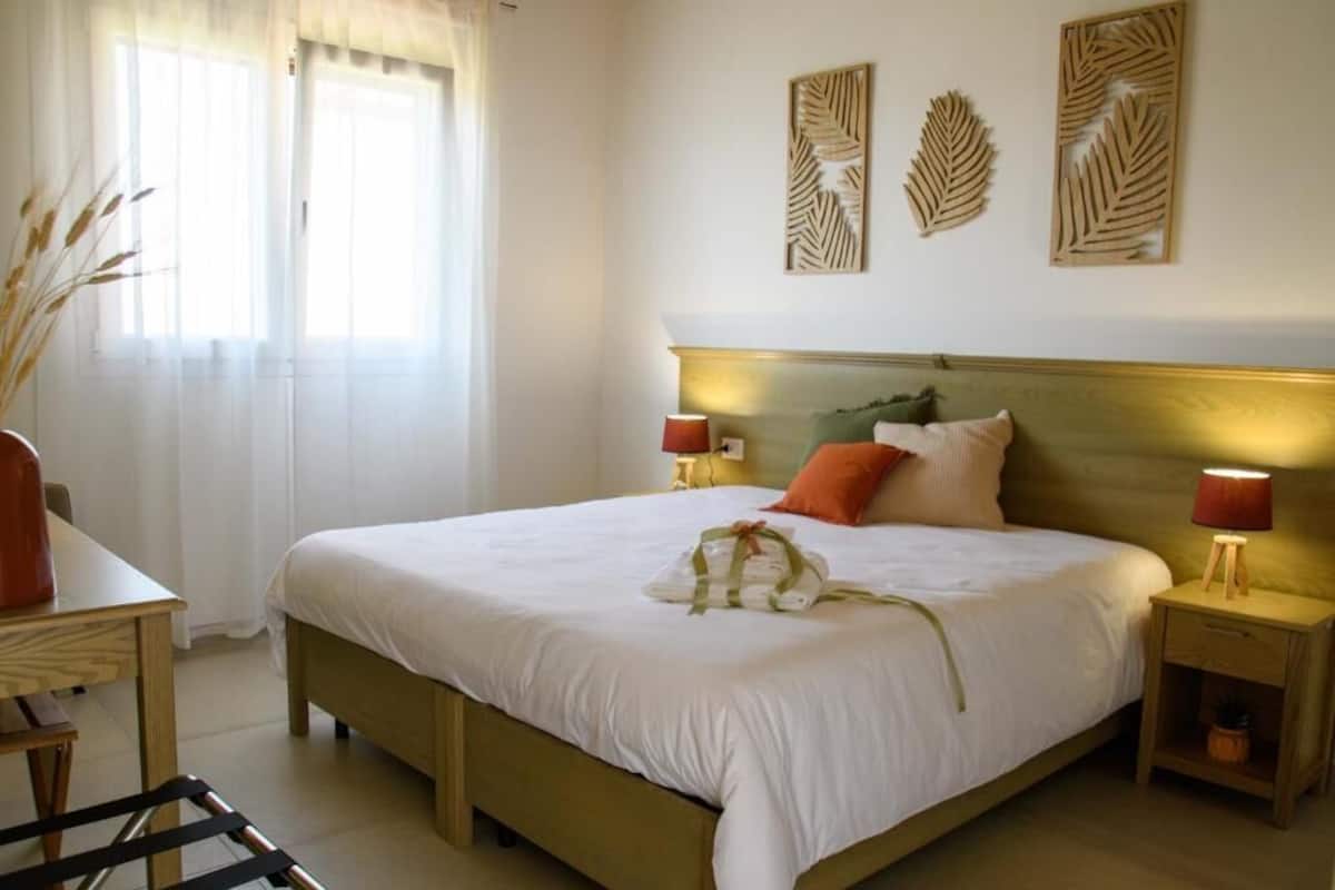 Uma cama bem arrumada com cabeceira, duas luminárias de mesa e um travesseiro decorativo.