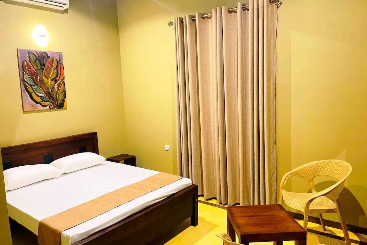 Quarto de hotel com cama, uma cadeira, uma mesinha e cortinas.