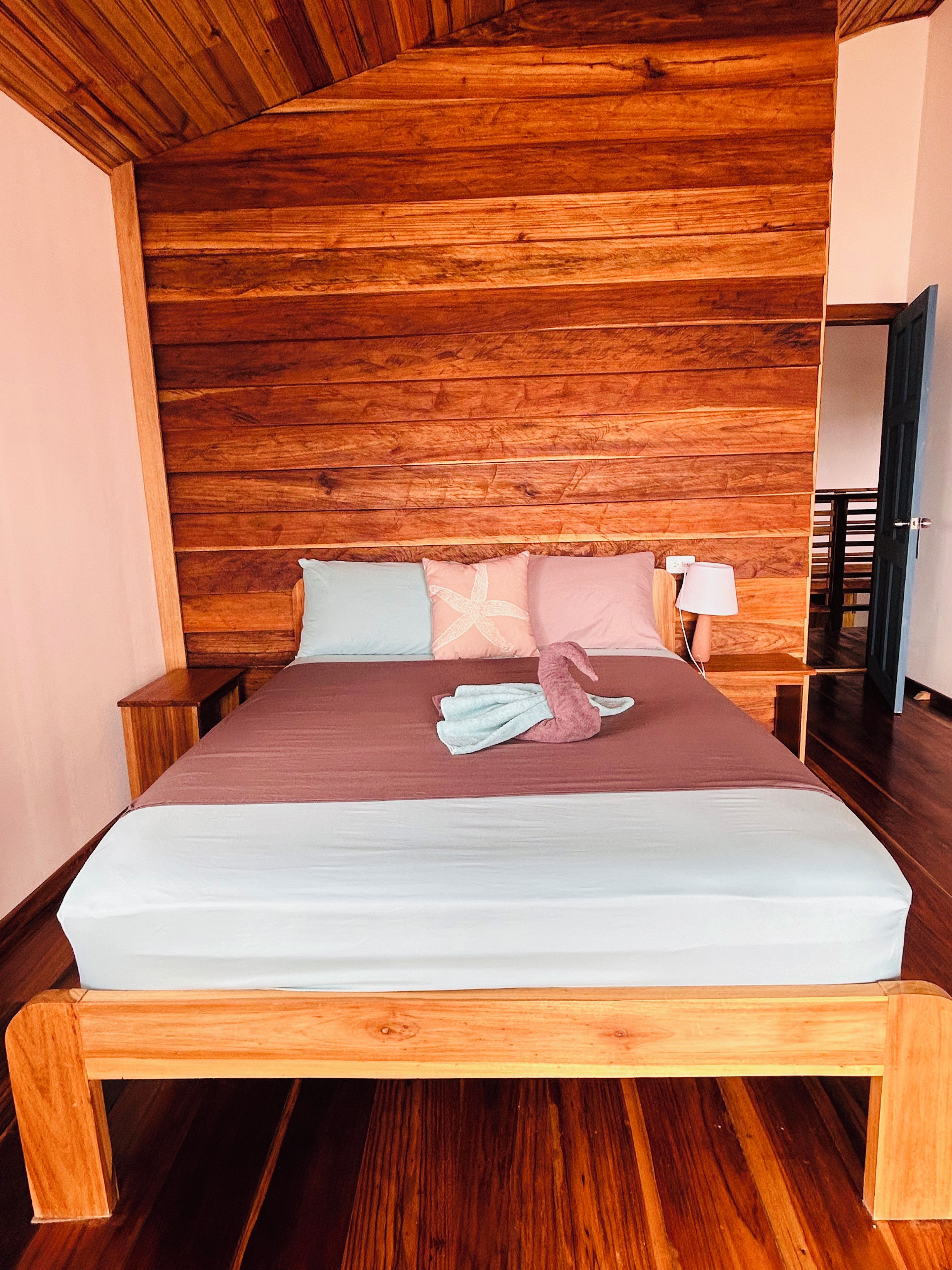 Uma cama de madeira com estrutura em madeira, colchão marrom, almofadas brancas e um travesseiro decorativo com a forma de cisne.