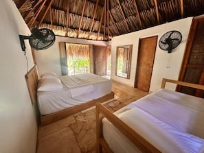 Quarto com duas camas de madeira, telhado de palha e dois ventiladores fixados na parede.