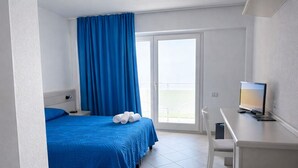 Quarto de hotel com uma cama, uma escrivaninha, uma cadeira e vista através de uma porta de correr.