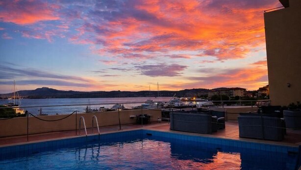 Piscina com vista para o mar e barcos ao pôr do sol.