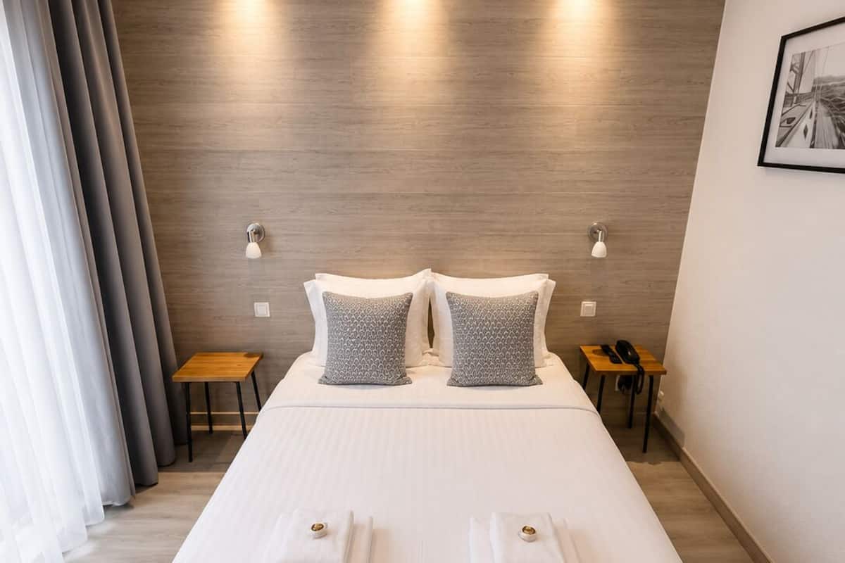 Quarto de hotel com uma cama grande, duas mesas de cabeceira, uma luminária na parede e um quadro emoldurado.