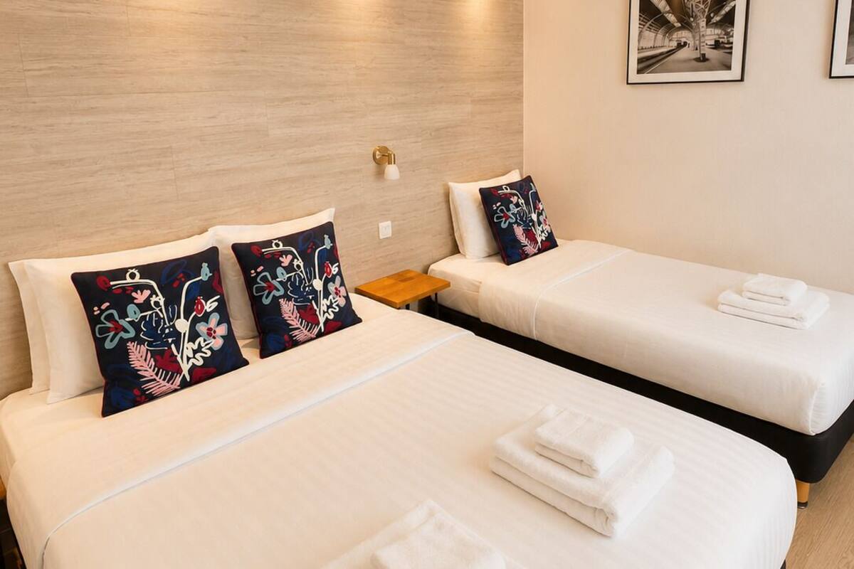 Quarto de hotel com duas camas, uma cabeceira de madeira, uma pequena mesa de madeira e duas imagens emolduradas na parede.