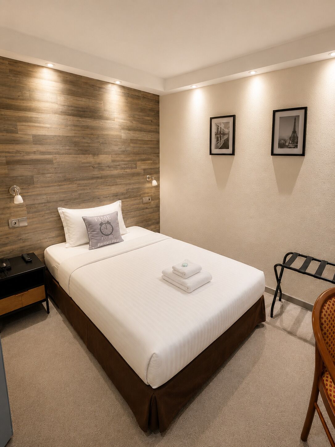 Quarto de hotel bem arrumado, com uma cama grande, mesa de cabeceira, uma cadeira e duas luminárias fixadas na parede.