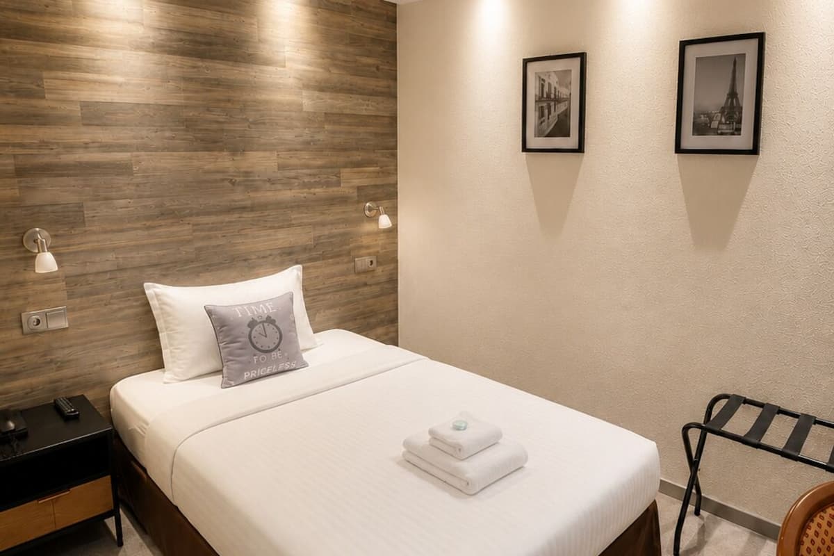 Quarto de hotel bem arrumado, com uma cama grande, mesa de cabeceira, uma cadeira e duas luminárias fixadas na parede.