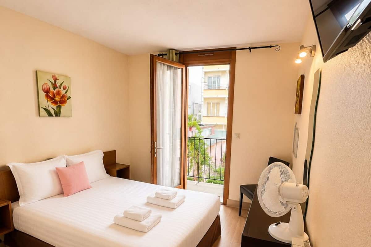 Quarto de hotel com uma cama, um radiador, um ventilador e vista para o exterior.