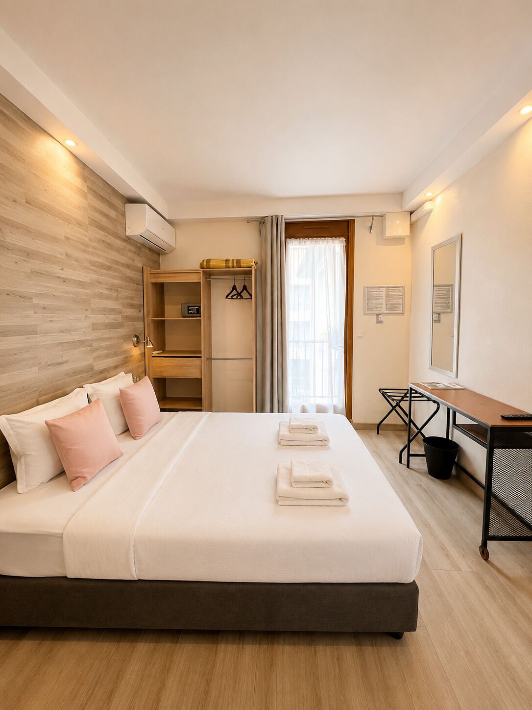 Quarto de hotel com uma cama grande, uma escrivaninha, um guarda-roupa e um espelho.