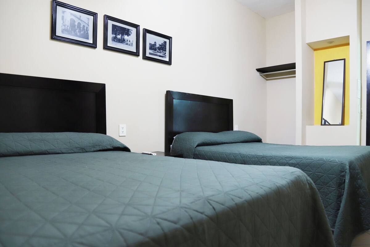 Quarto de hotel com duas camas, televisão na parede e três quadros emoldurados.
