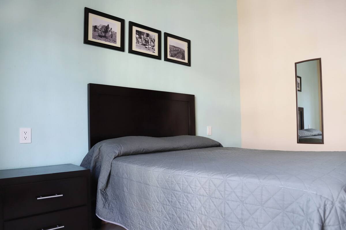Quarto com uma cama, mesa de cabeceira, cômoda e três quadros na parede.
