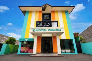 Fachada de hotel com design de faixa vertical colorida, placa com o nome 'Hotel Fiducia' e logotipo indicando ser um hotel da coleção.