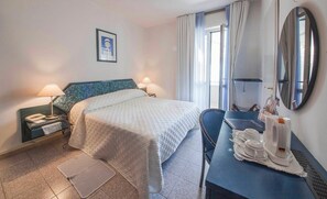 Quarto de hotel com cama, abajures, uma escrivaninha e um espelho.