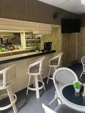 Uma área de bar com cadeiras de vime, um balcão com garrafas e uma televisão fixada na parede.