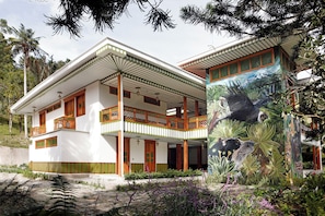 Um edifício de dois andares com varanda, um mural e um jardim.