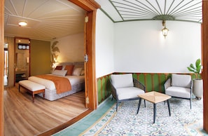 Quarto com uma cama, duas cadeiras, uma mesinha e um ventilador de teto decorativo.