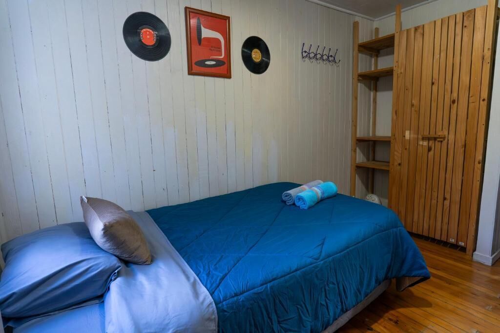 Quarto com uma cama, um guarda-roupa de madeira e decorações nas paredes, incluindo discos de vinil e um letreiro.