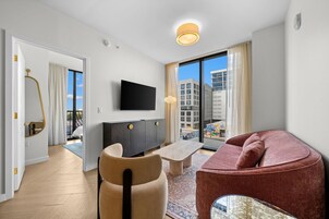 Uma sala de estar moderna com televisão de tela plana, sofá, mesa de centro e vista para a cidade.