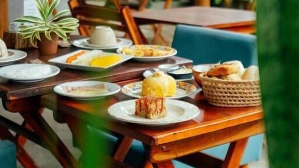 Uma área de refeições com mesas, cadeiras, pratos com comida e uma cesta de pão.