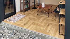 Quarto compacto com piso de madeira, televisão integrada, pequena mesa e área de estar com bancos.