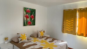 Quarto com cama, mesa de cabeceira, um quadro na parede e janela com cortinas.