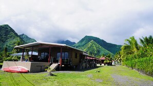 Um edifício com área externa coberta, degraus de acesso e vista para montanhas verdes ao fundo.