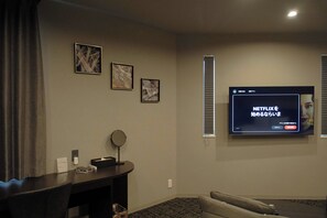 Quarto com televisão na parede, uma mesa pequena com um espelho e quadros pendurados na parede.