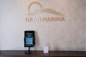 Uma receção com um ecrã digital a exibir uma mensagem de boas-vindas e uma placa com o nome 'GRAN MARINA'.