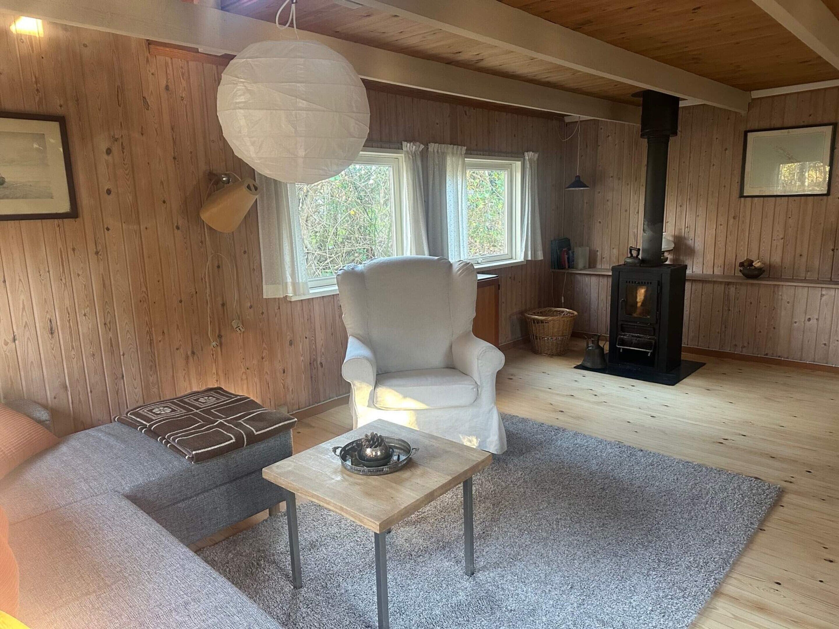 Interior acolhedor de uma cabana com sofá, poltrona, mesa e lareira a lenha.