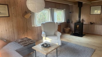 Interior acolhedor de uma cabana com sofá, poltrona, mesa e lareira a lenha.