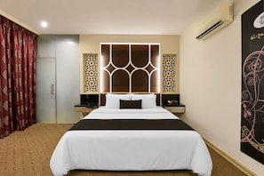 Quarto de hotel com uma cama grande, um guarda-roupa, um aparelho de ar condicionado e painéis decorativos na parede.