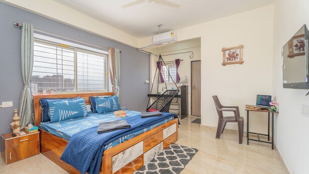 Um quarto com cama, escrivaninha, cadeira, janela e ventilador de teto.