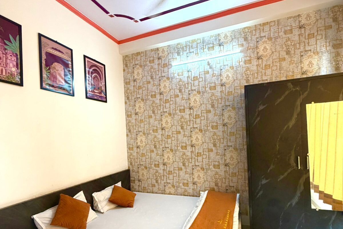 Quarto com cama, ventilador de teto, papel de parede estampado e quadros nas paredes.