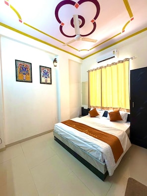 Quarto com cama, ventilador de teto, duas luminárias fixadas na parede, janela com cortinas e porta.