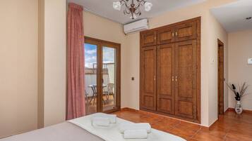 Um quarto com cama, guarda-roupa, varanda com cadeiras e uma luminária no teto.