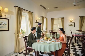 Uma sala de jantar com chão quadriculado, uma mesa redonda com toalha verde e cadeiras.