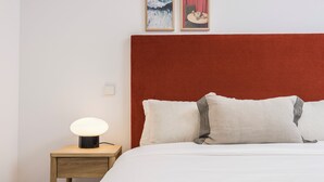 Uma cama com roupa de cama branca, cabeceira vermelha e duas imagens emolduradas na parede.