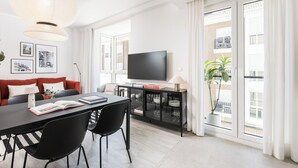 Uma sala de estar moderna com área de jantar, televisão de tela plana e grandes janelas com cortinas.