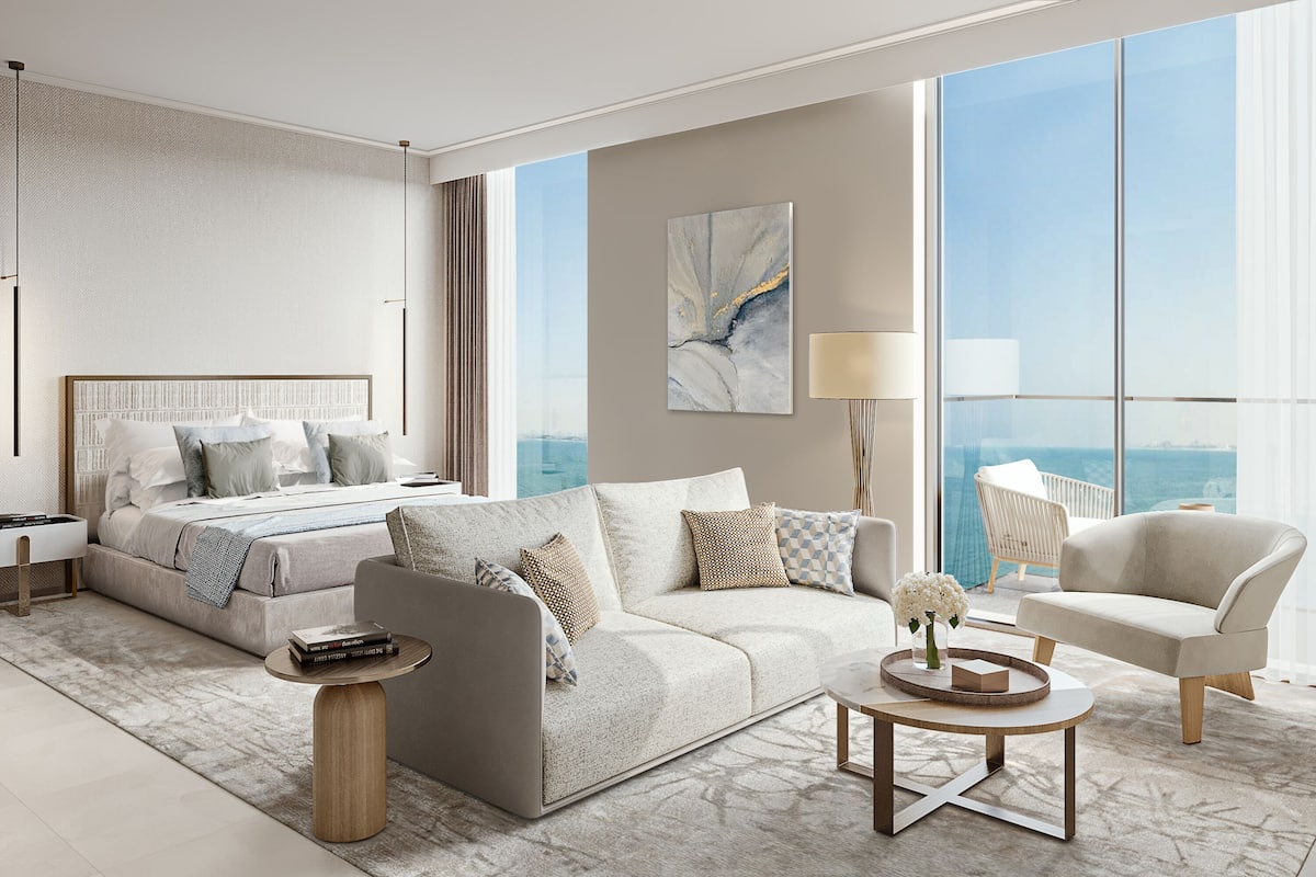 Quarto de hotel moderno com cama, sofá, poltrona e mesa de centro redonda.