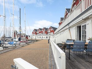 Marina com barcos atracados, um deck de madeira com cadeiras e um edifício com fachada vermelha e branca.
