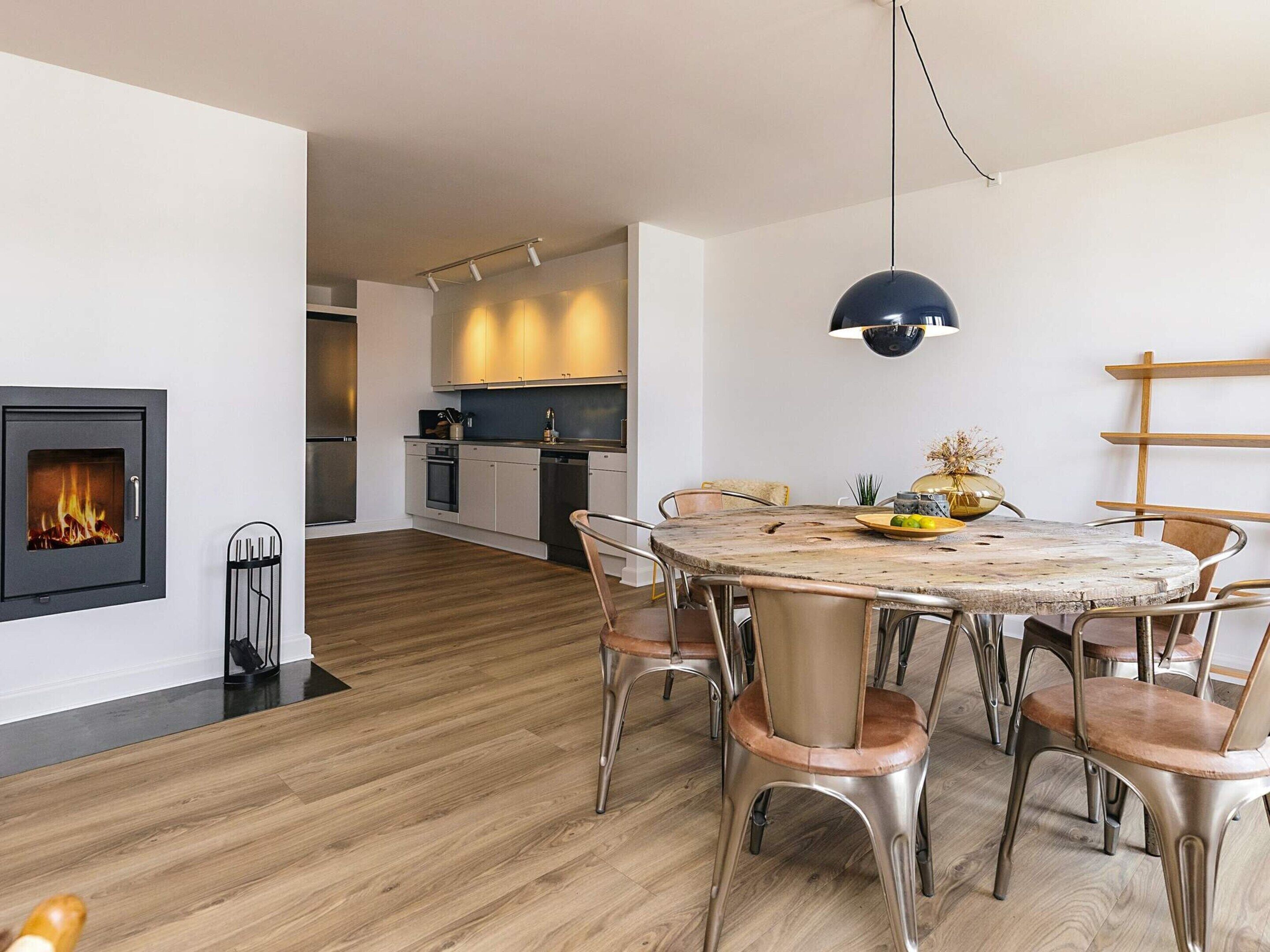 Uma cozinha moderna com fogão embutido, área de jantar com mesa redonda e cadeiras de metal, e uma luminária pendente.