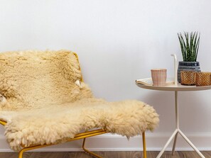 Um quarto com uma poltrona bege e fofa, uma mesa redonda pequena com uma planta em vaso e uma xícara estampada.