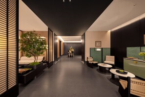 Um corredor moderno com um sofá, uma mesinha, uma cadeira e uma planta.