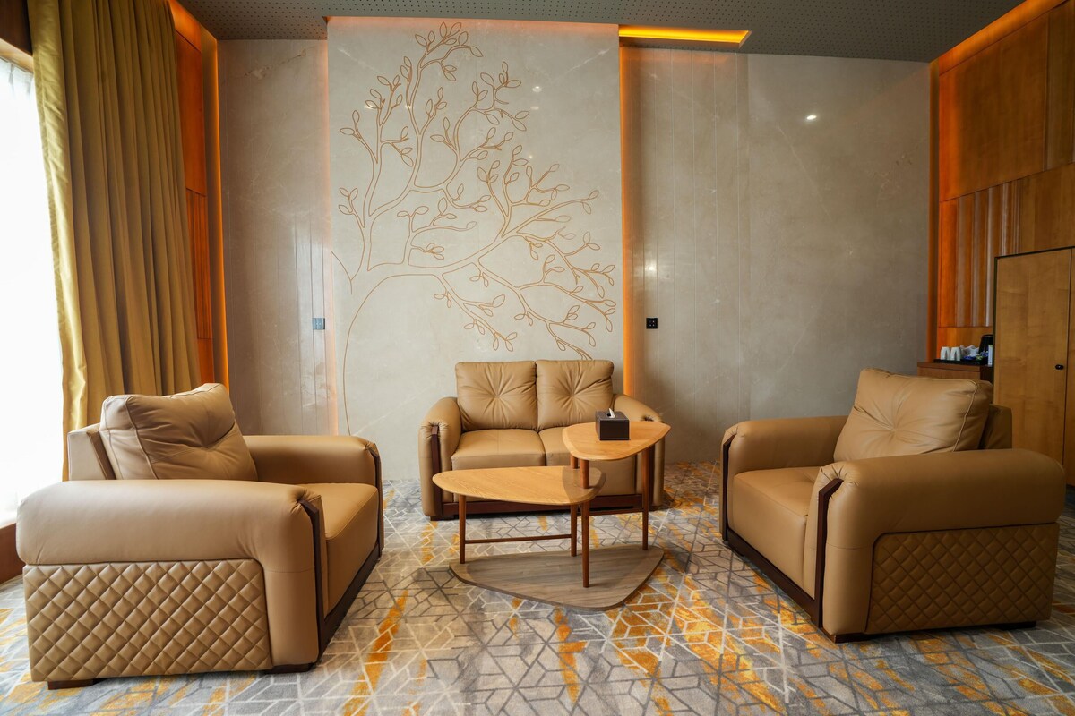 Uma sala de estar moderna com sofás de couro, uma mesa de centro e uma parede decorativa com o desenho de uma árvore.