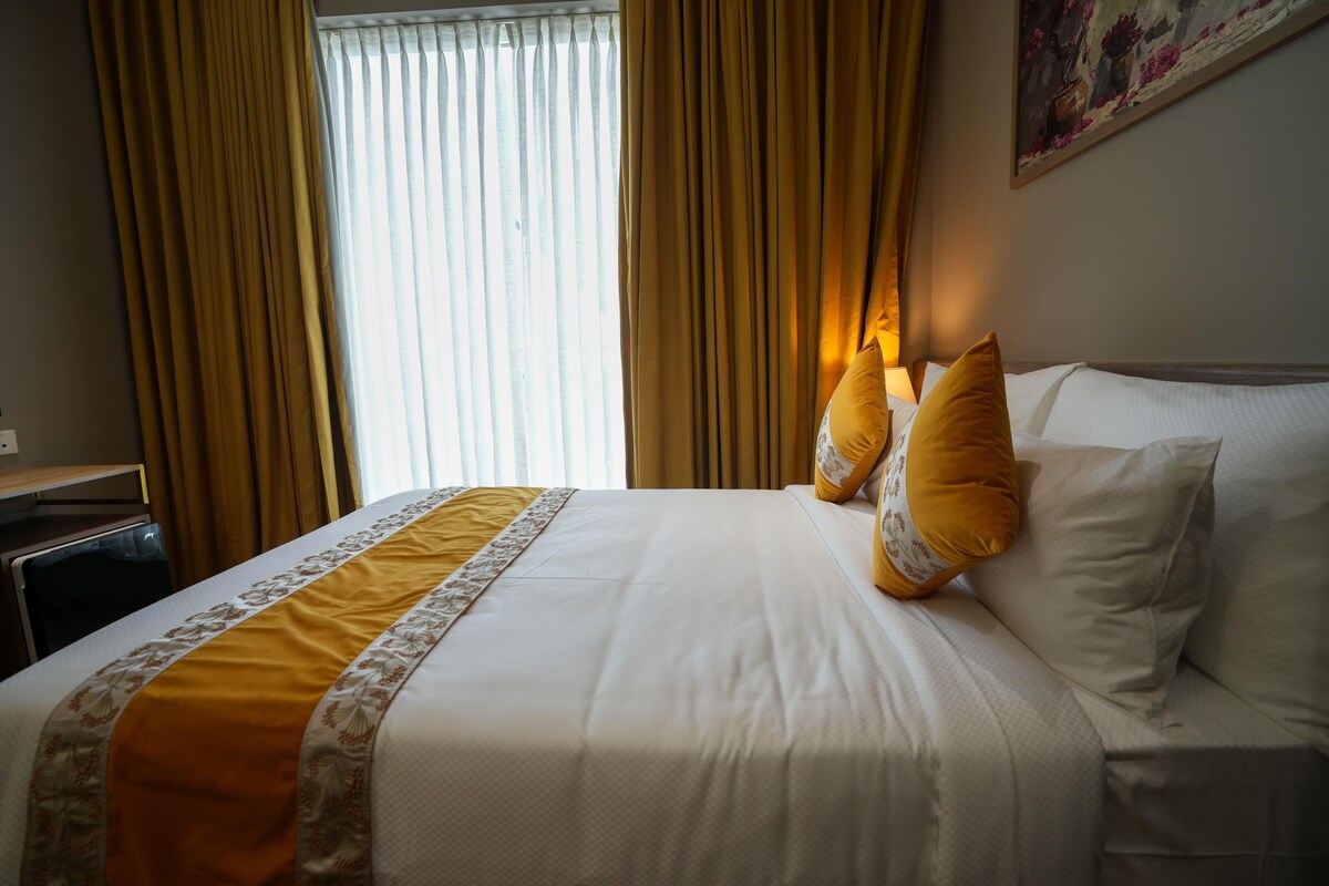 Quarto de hotel com cama, cortinas, um quadro e uma escrivaninha.