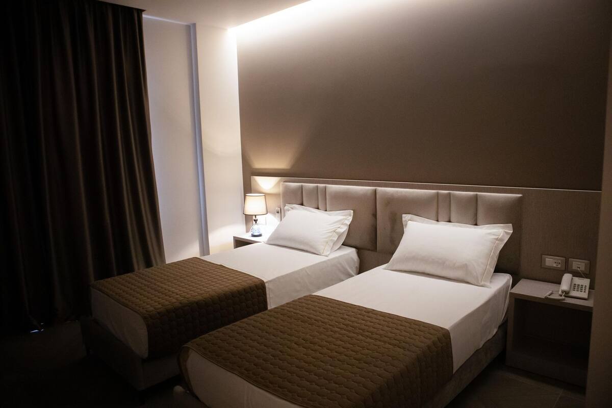 Quarto de hotel com duas camas, uma mesa de cabeceira com abajur e um telefone.
