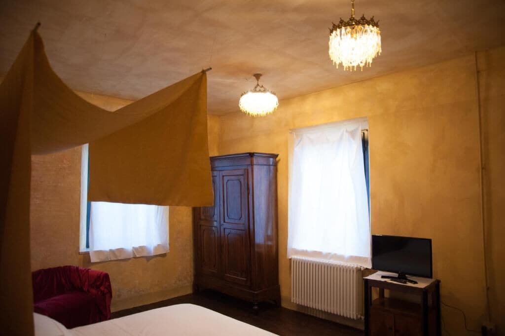 Quarto com uma cama, televisão sobre uma mesinha, armário e um candelabro.